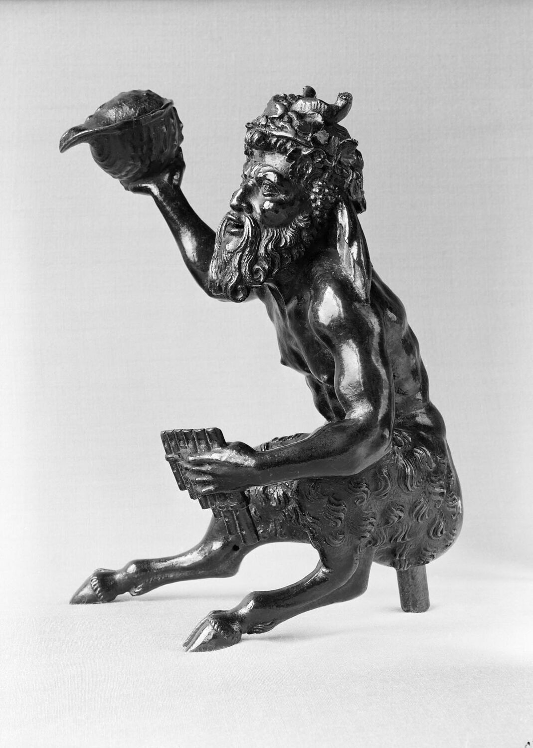 Statuette : satyre assis, les pattes écartées, tenant de sa main droité ...